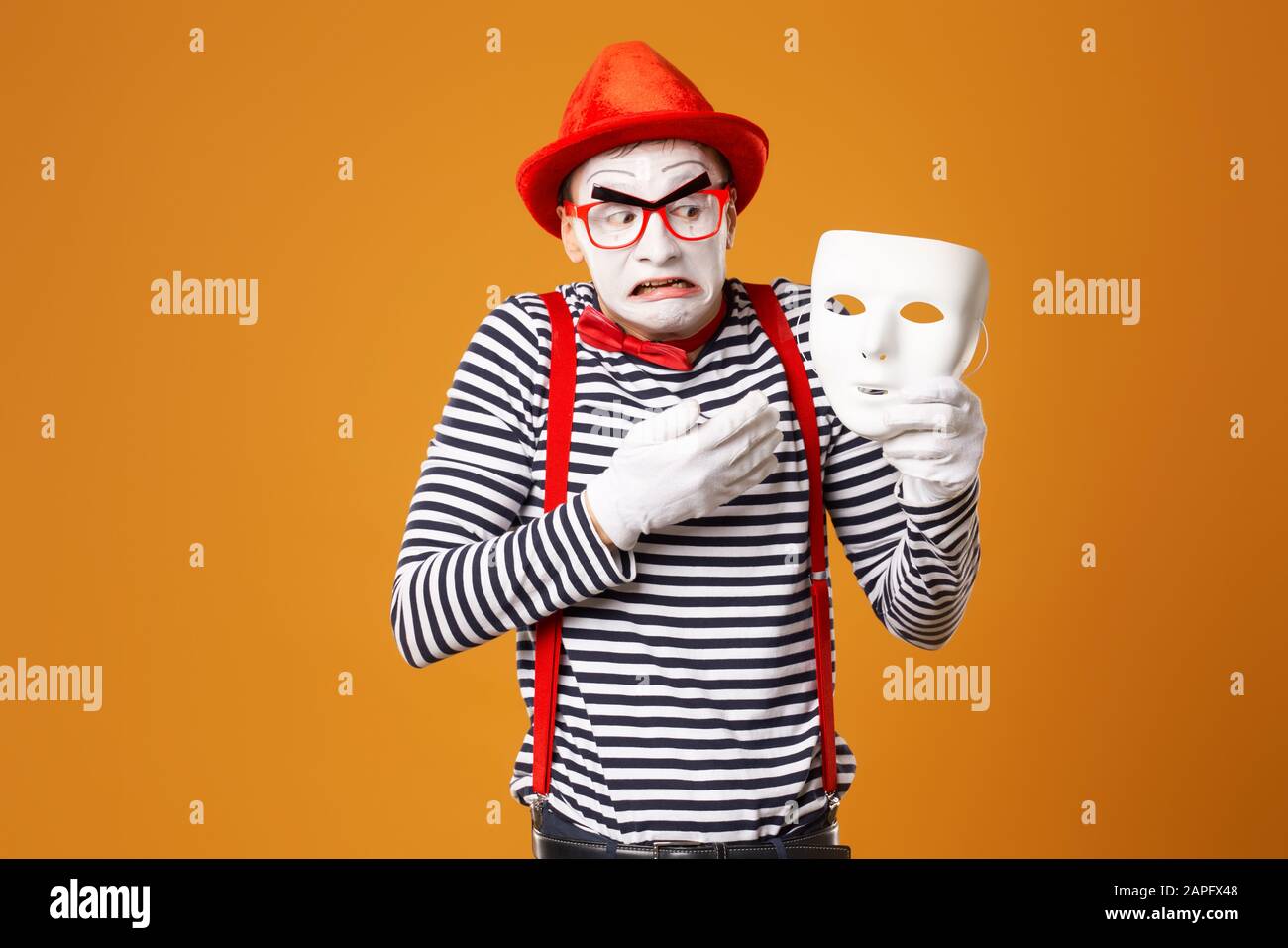 Sad mime in red hat and in vest with white mask on blank orange ...