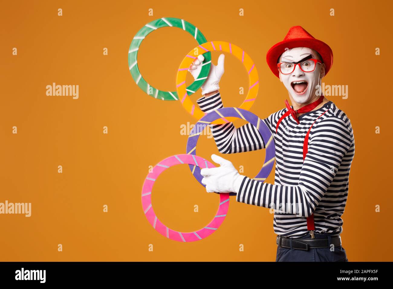 Happy mime man with multi-colored rings on empty orange background ...