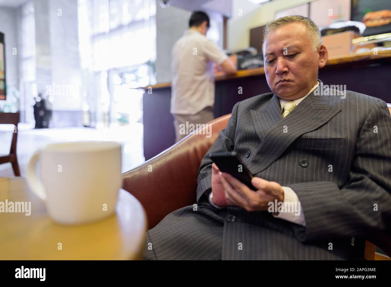 Portrait of mature Japanese businessman relaxing inside the coffee shop ...