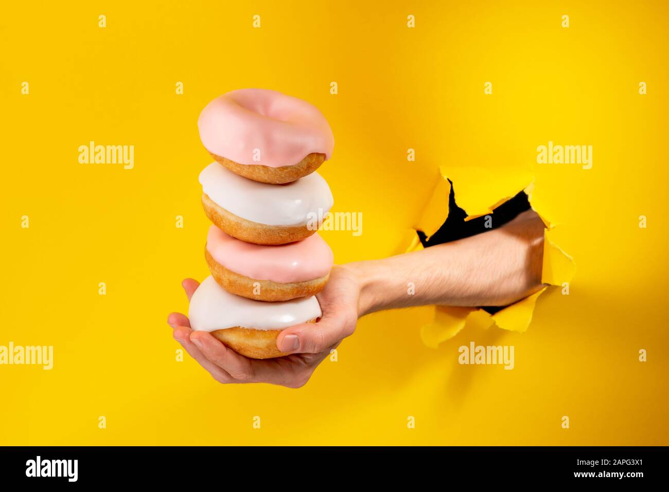 Hand holding a pile of fresh donuts and giving them through a torn hole ...