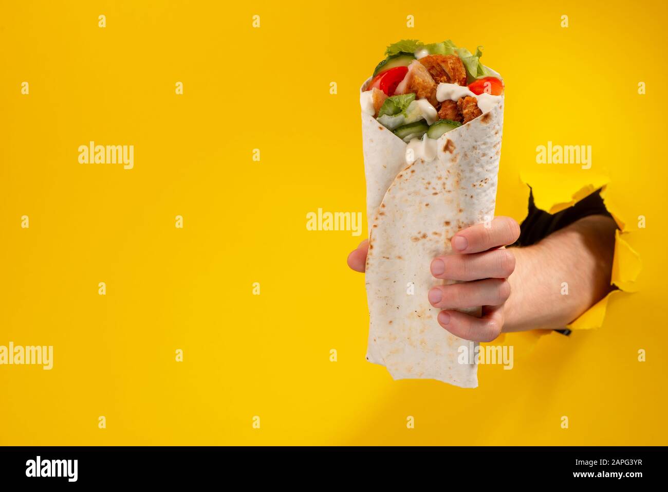 Hand giving a doner roll through a torn hole in yellow paper background ...