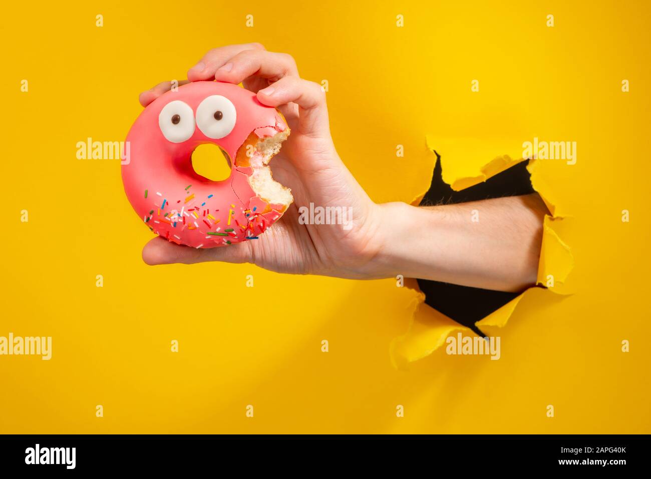 Hand showing a bitten pink donut with scared sugar eyes Stock Photo - Alamy