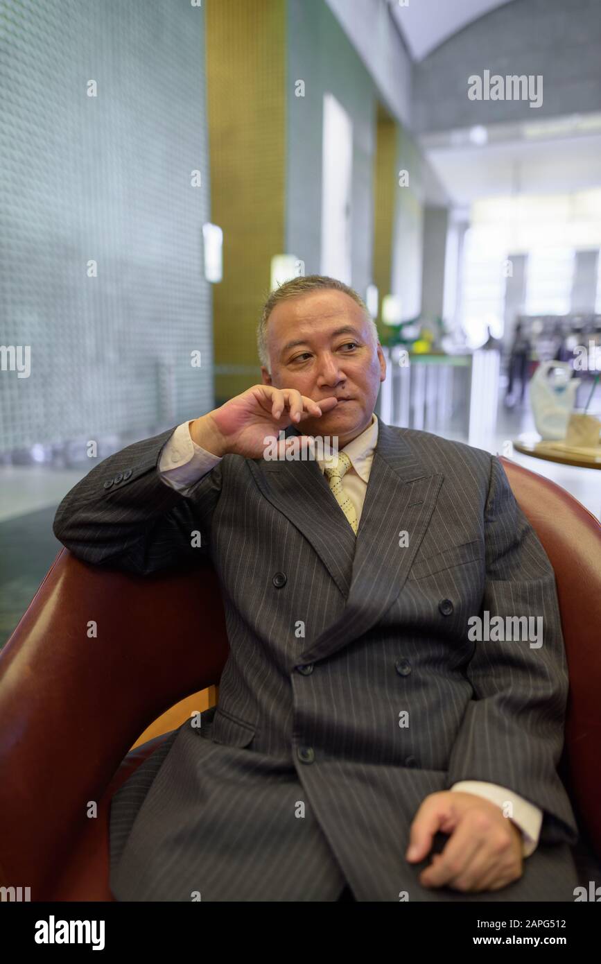Portrait of mature Japanese businessman relaxing inside the coffee shop ...
