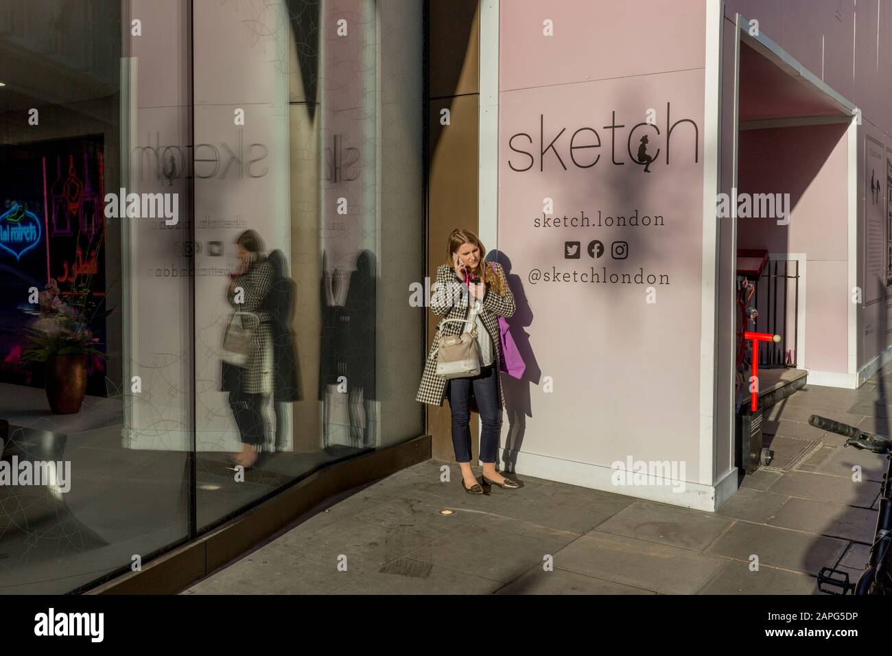 A young woman holds a private phone conversation in a sunny corner next ...