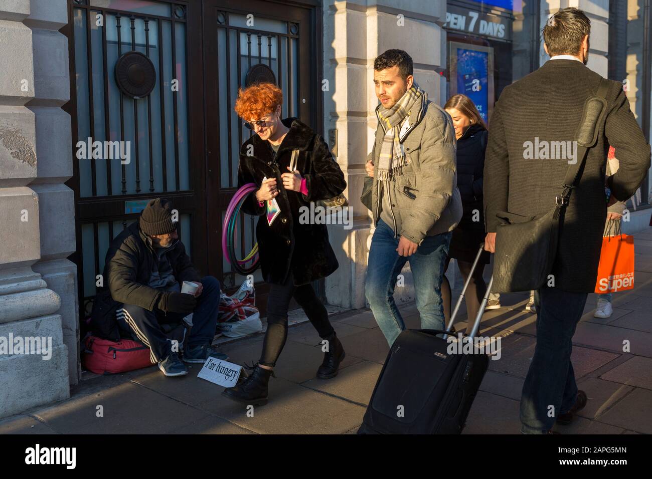 Passers-by ignore a homeless man begging with a sign saying 'I'm hungry ...