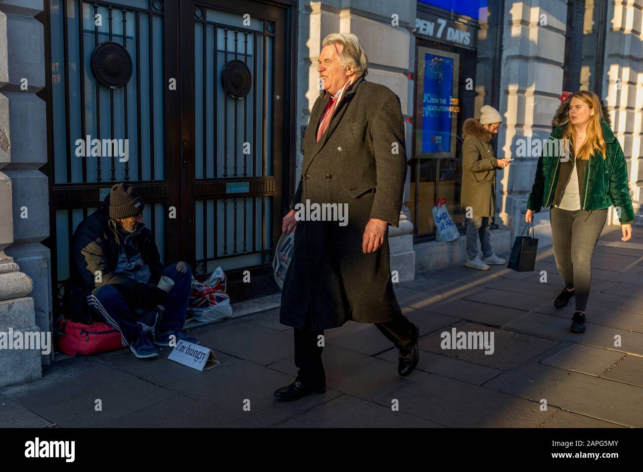 Passers-by ignore a homeless man begging with a sign saying 'I'm hungry ...
