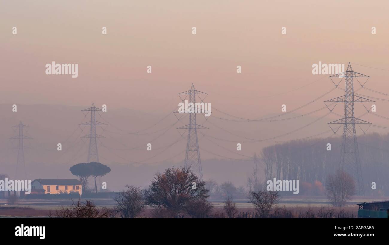 Electric pylons covered in fog and smog shortly after the dawn of a new ...