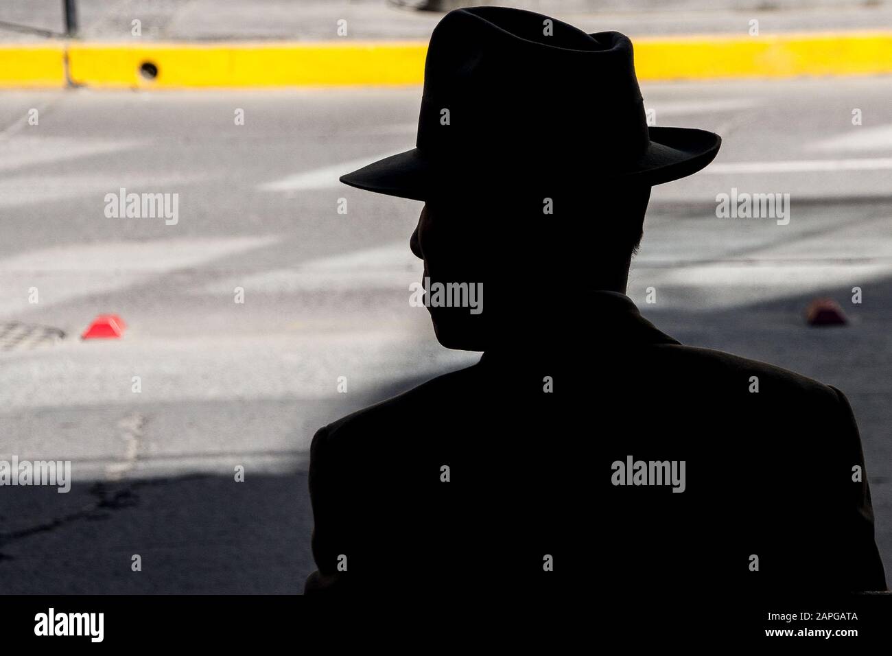 Silhouette of a male wearing a hat standing in the shadow by the street ...