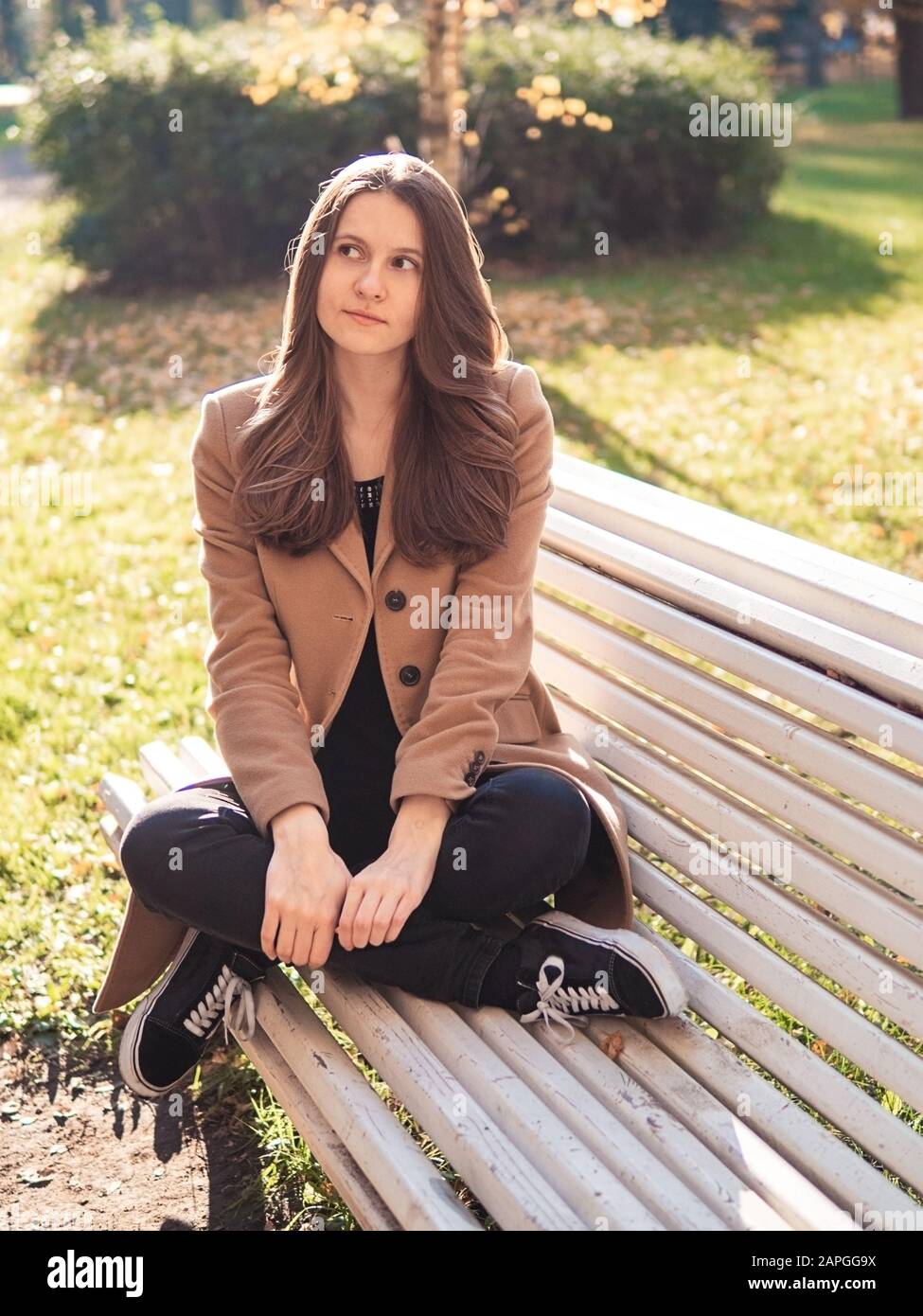 Beautiful teen girl sitting in the Park on a bench, dreaming, thinks ...