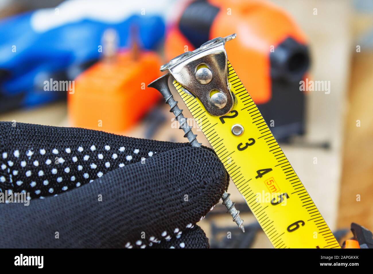 The black screw in hand and is measured by a yellow tape measure with a ...
