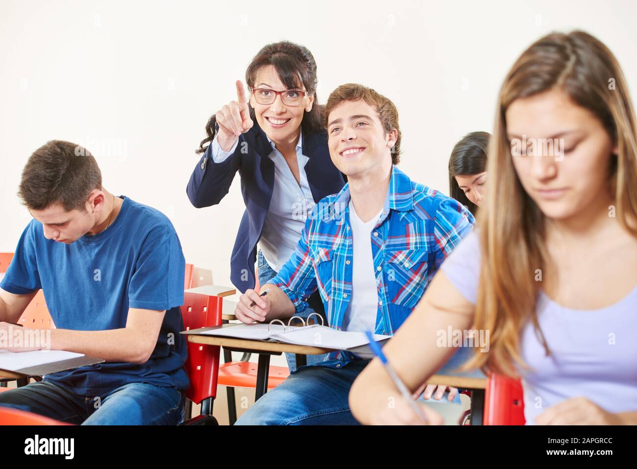 Teacher helps students in class at school Stock Photo - Alamy
