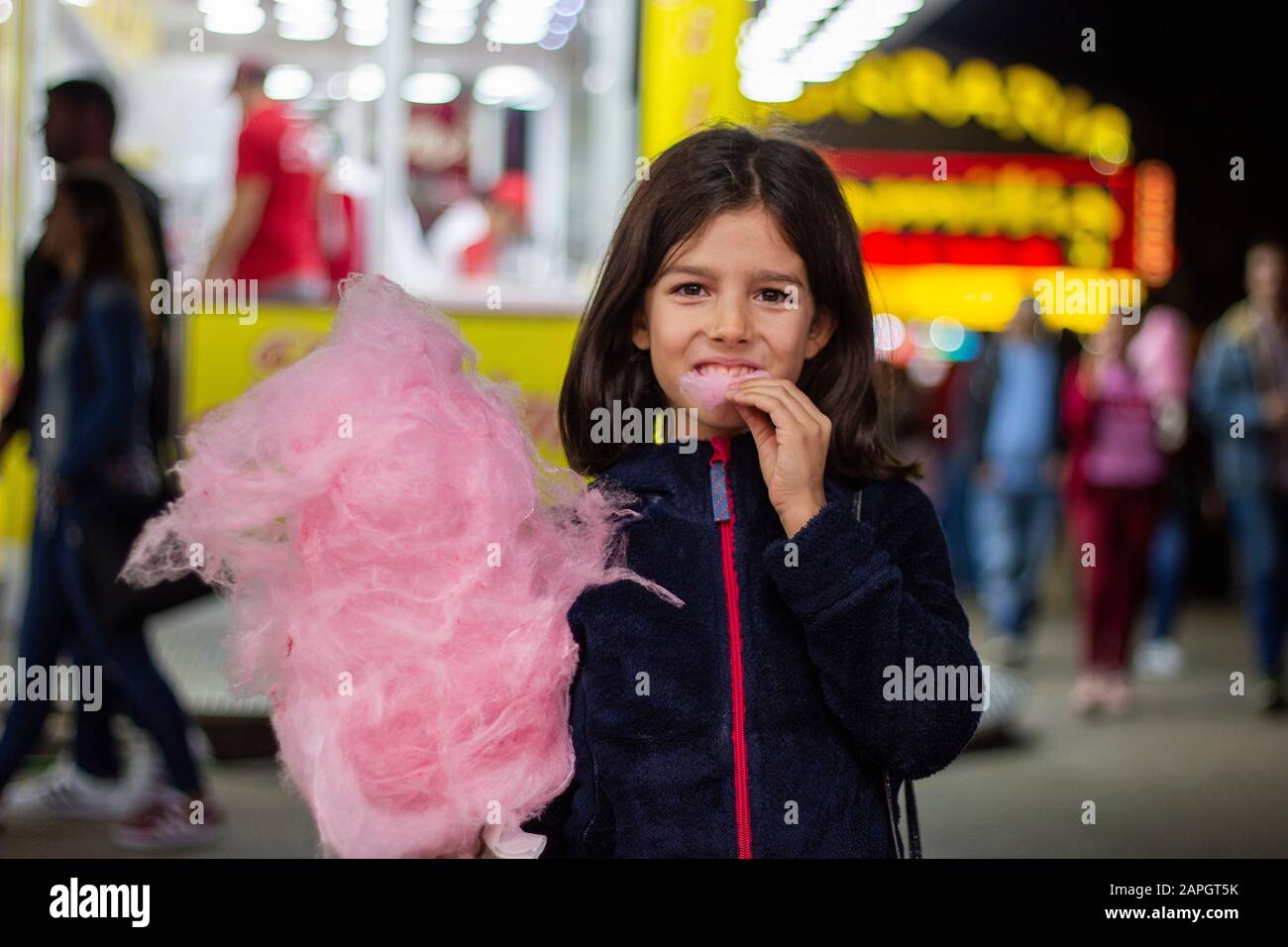 Cute girl eating a big ball of cotton candy on a amusement park Stock ...