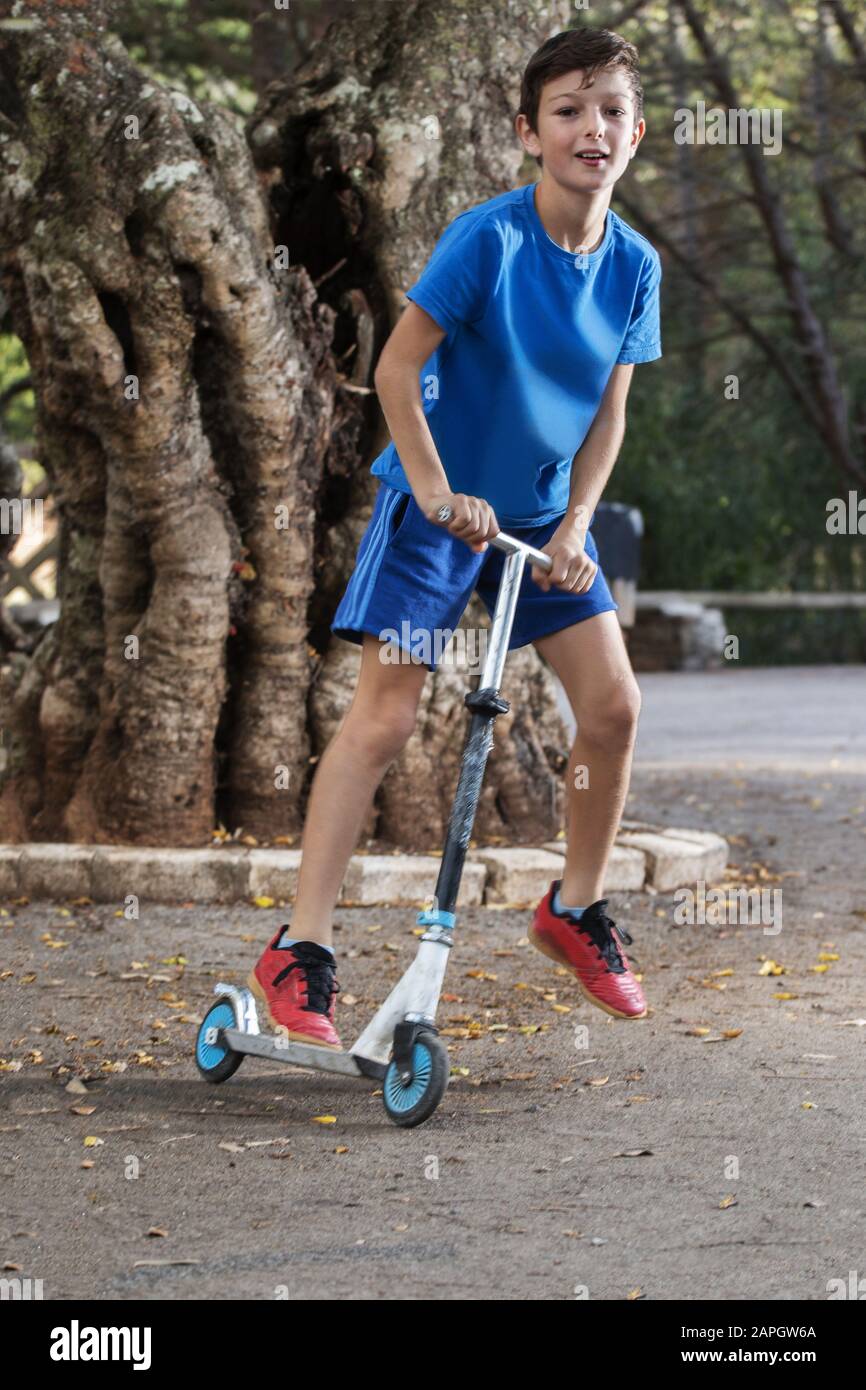 Cute boy with skate scooter performing stunts Stock Photo - Alamy