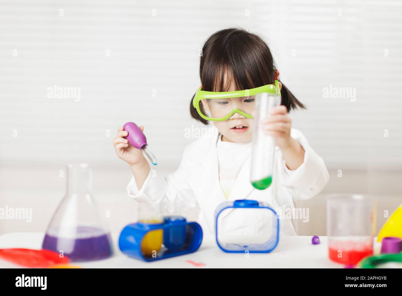 toddler girl pretend play scientist role at home against white ...