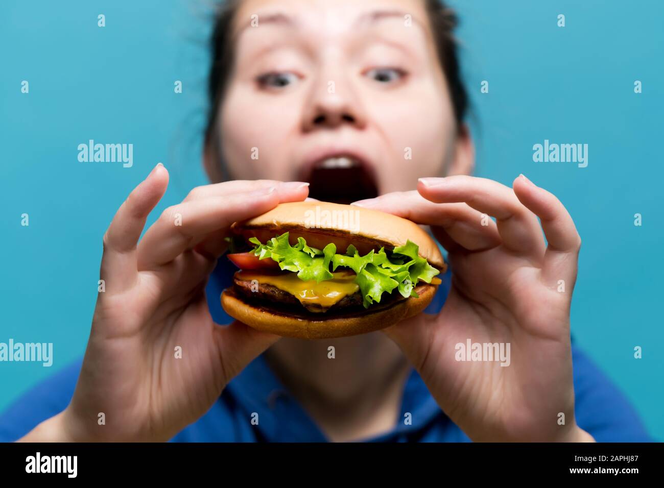 the girl opened her mouth and is going to eat her burger, which she ...
