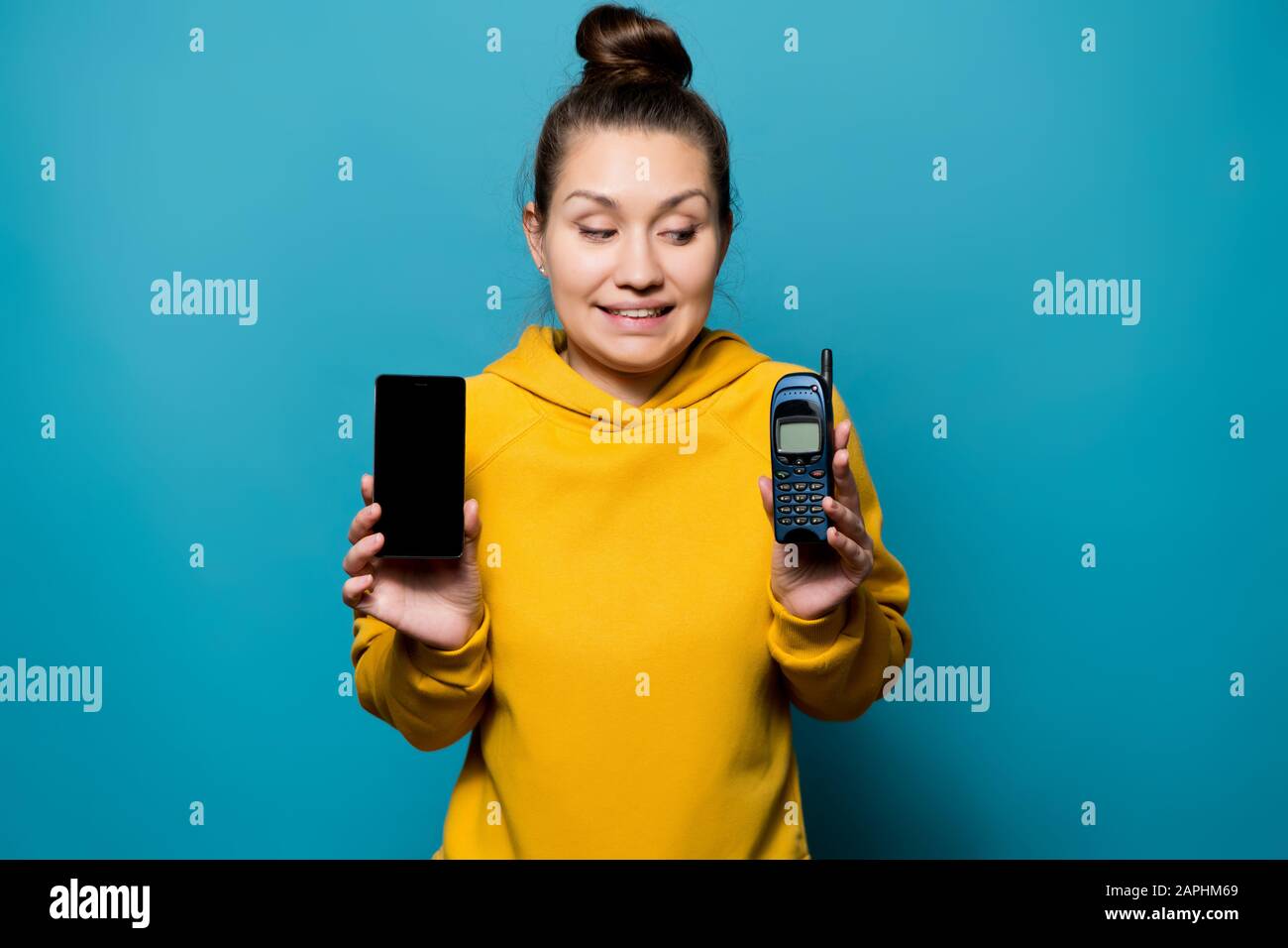 young woman shows an old phone with buttons and a smartphone, smiling ...