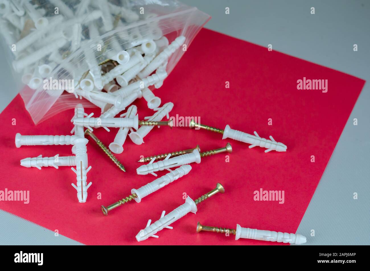Screws with plastic dowels on a red background. Group fasteners in a ...