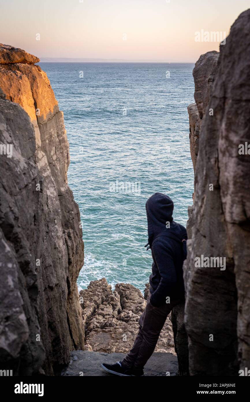 Young man leaning between two big rocks, looking to the ocean in the ...