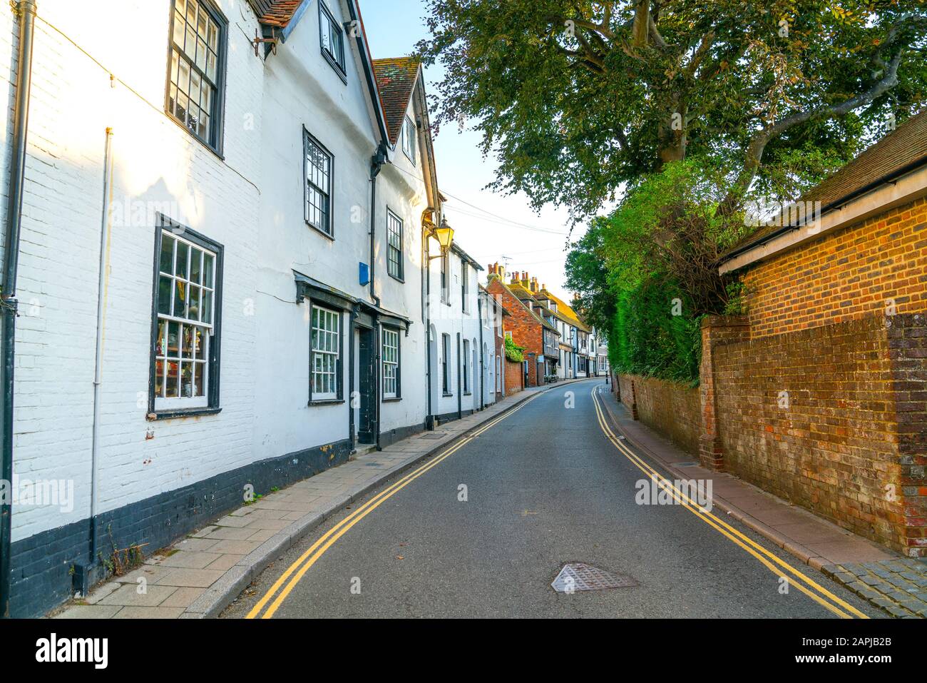 Shady narrow street with white and black buildings on one side and red ...