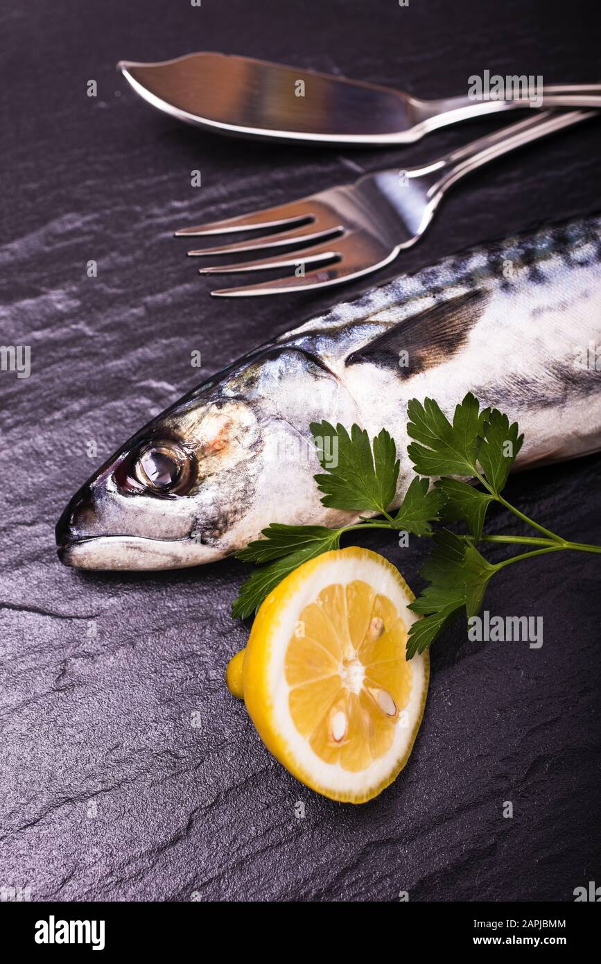 fresh sea fish on a slate stone ready to cook with lemon and cutlery ...