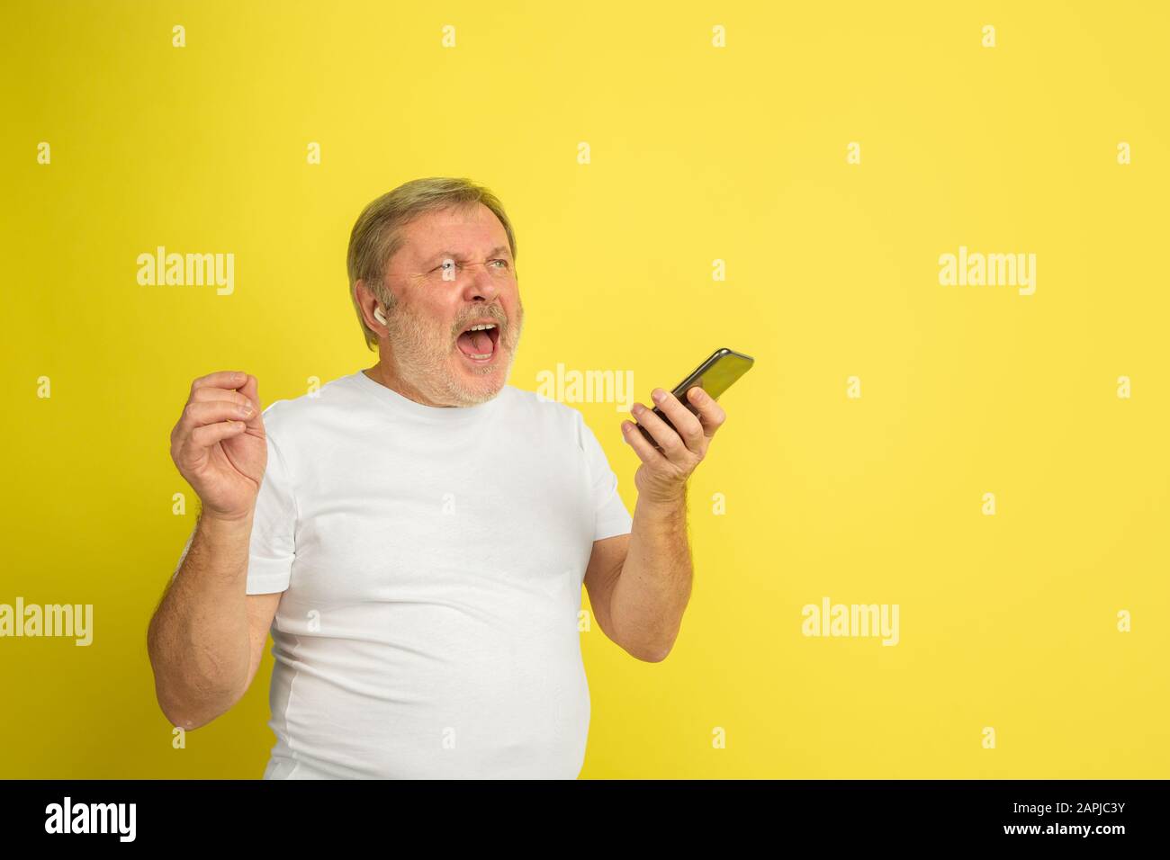 Singing with earphone and smartphone. Caucasian man portrait on yellow ...