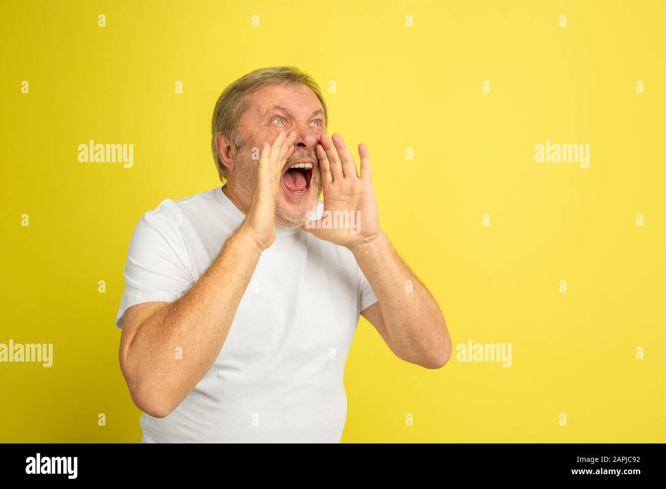 Calling, screaming. Caucasian man portrait isolated on yellow studio ...
