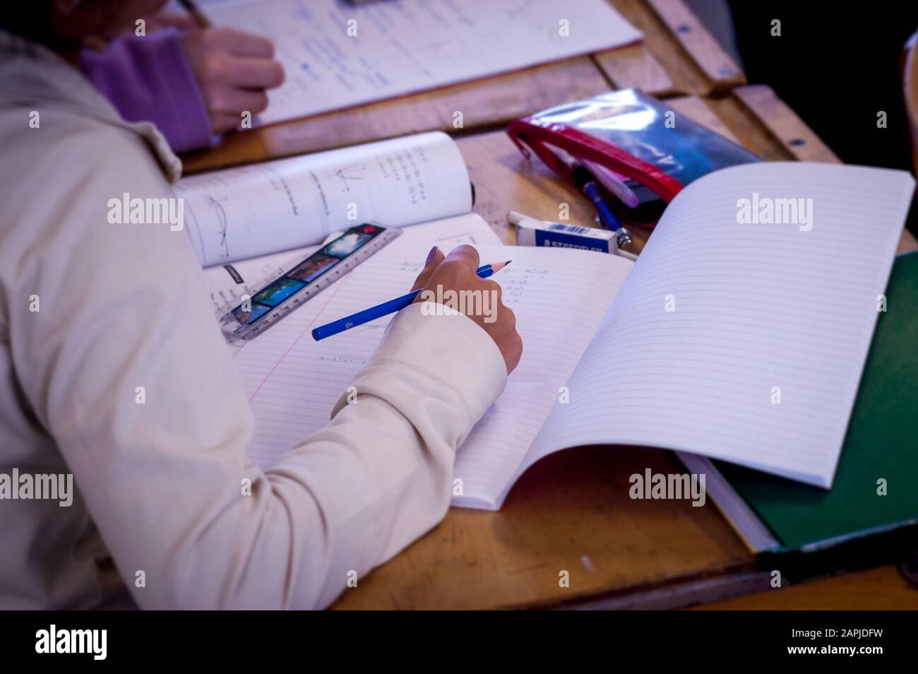 text books and exercise books on desk with pupil working in classroom ...