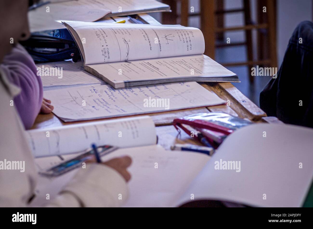 text books and exercise books on desk with pupil working in classroom ...