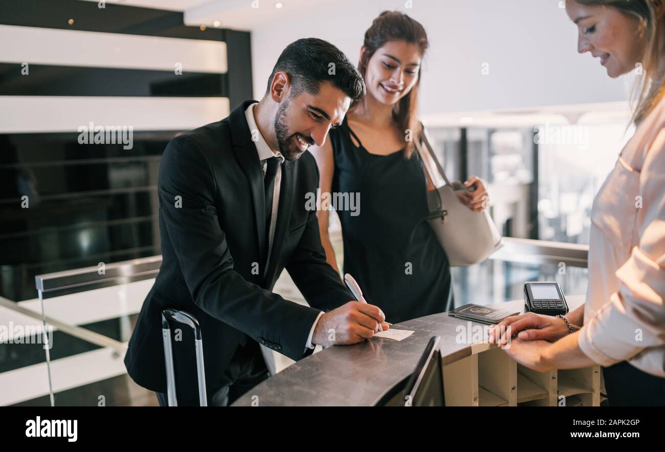Portrait of two young business people check-in at hotel reception front ...