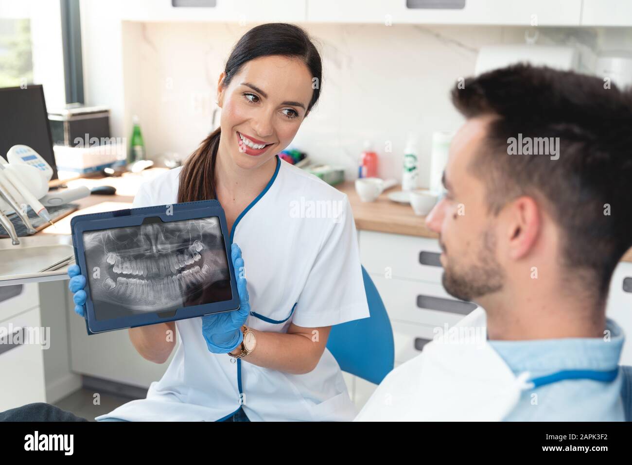 Female dentist showing teeth x-ray on digital tablet screen. Patient ...