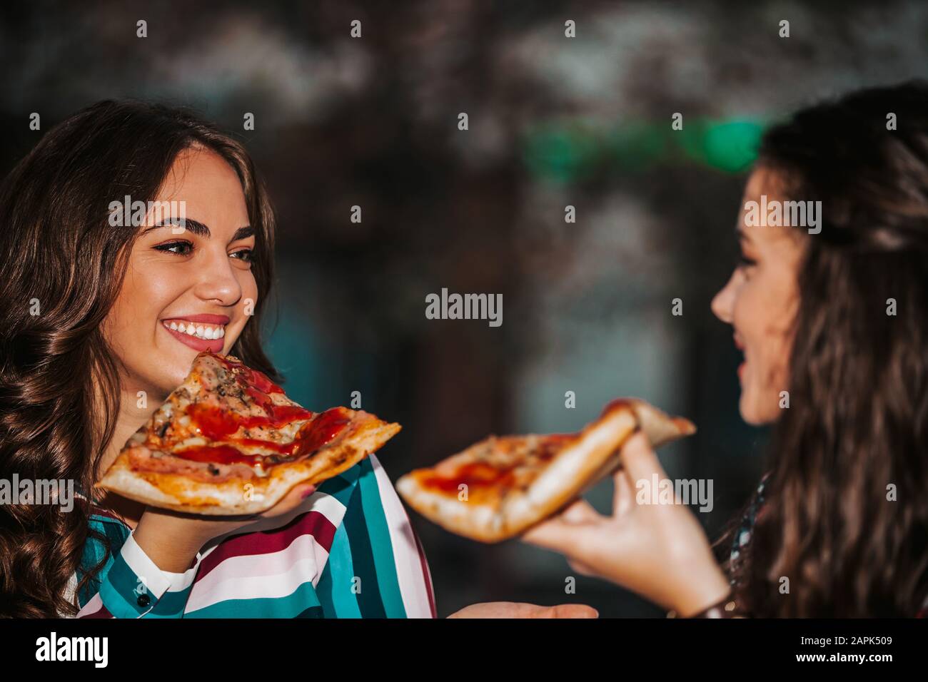 Portrait of two young women eating pizza outdoors, having fun together ...