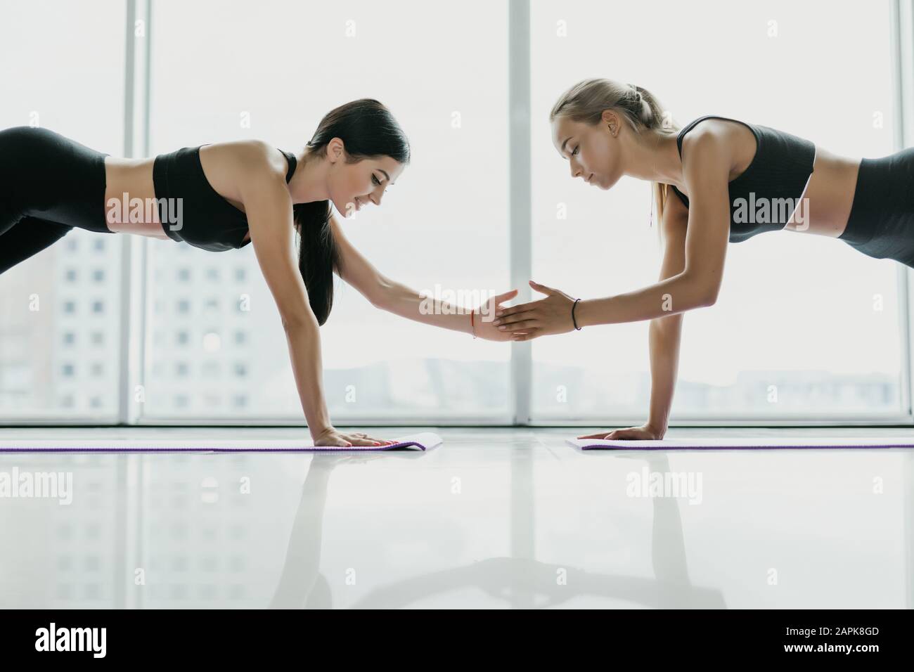Two young beautiful women giving high five while practicing basic plank ...