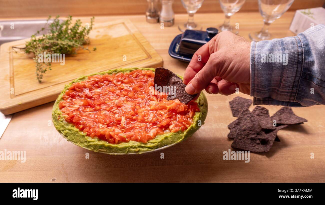 Casual middle aged man dipping into Mexican salsa dip while holding ...