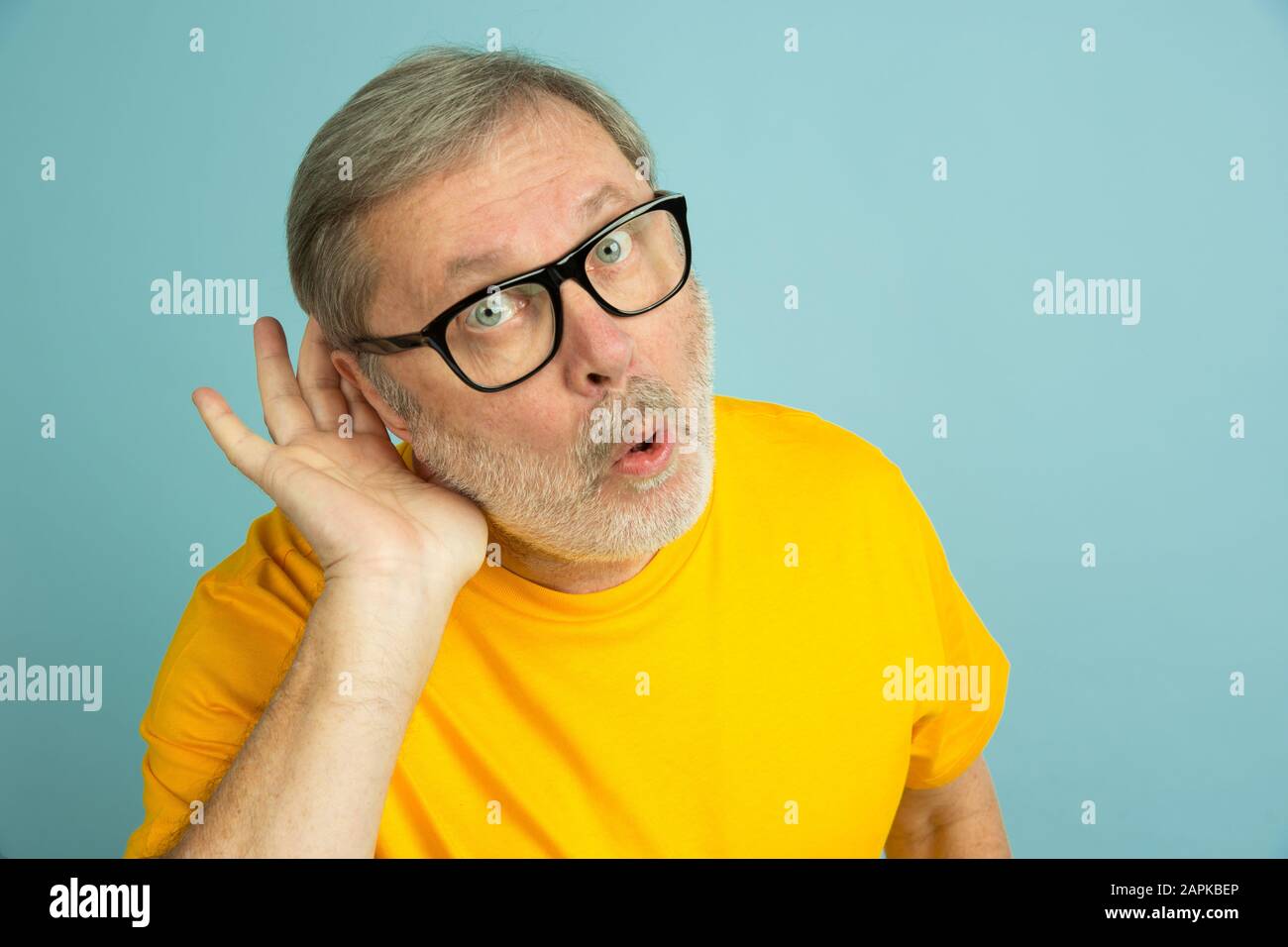 Listening to secrets with hand on ear. Caucasian man portrait on blue ...