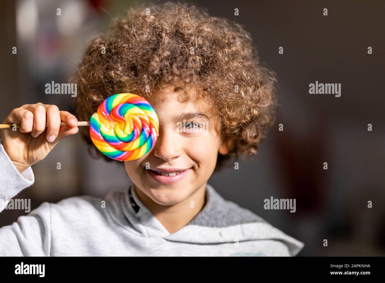 Portrait of smiling boy with brown ringlets covering eye with colourful ...