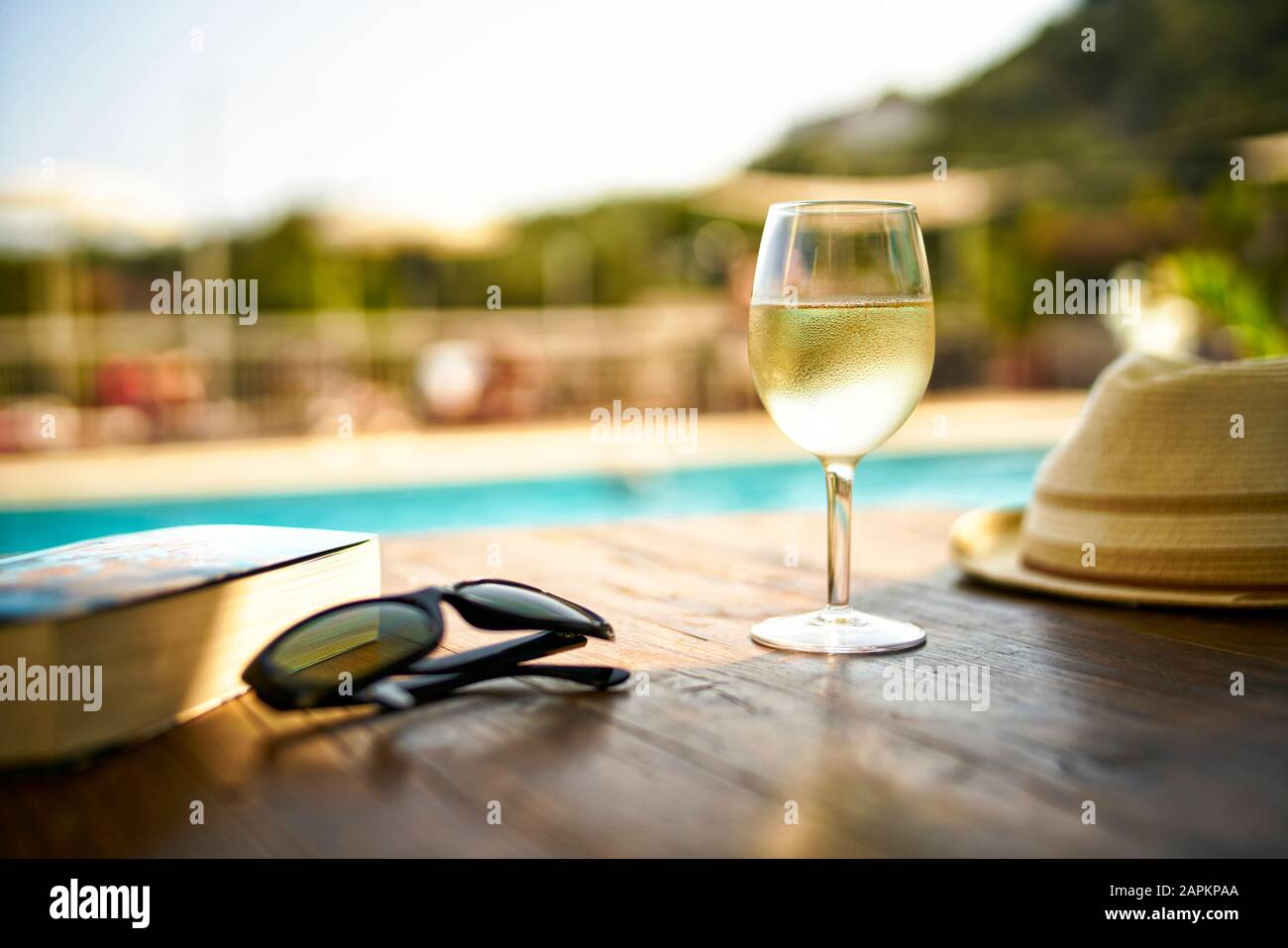 Glass of cooles white wine, book, sunglasses and straw hat in front of ...