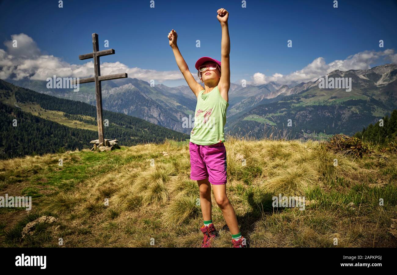 Girl standing at mountaintop in alpine scenery with raised arms ...