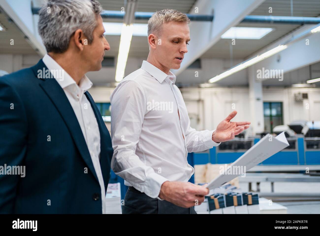 Two businessmen with paper talking in a factory Stock Photo - Alamy