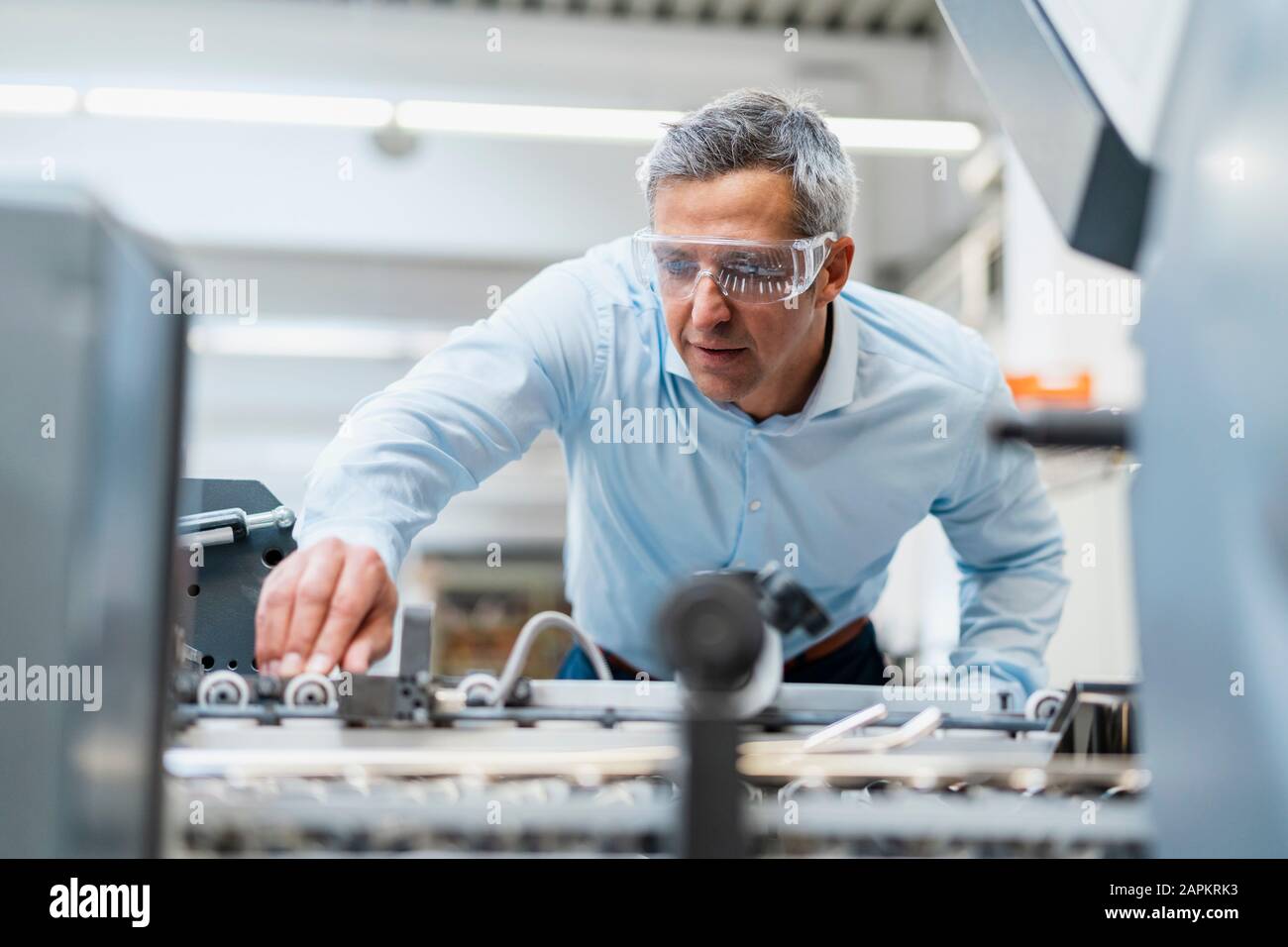 Man wearing safety goggles adjusting a machine in a factory Stock Photo ...