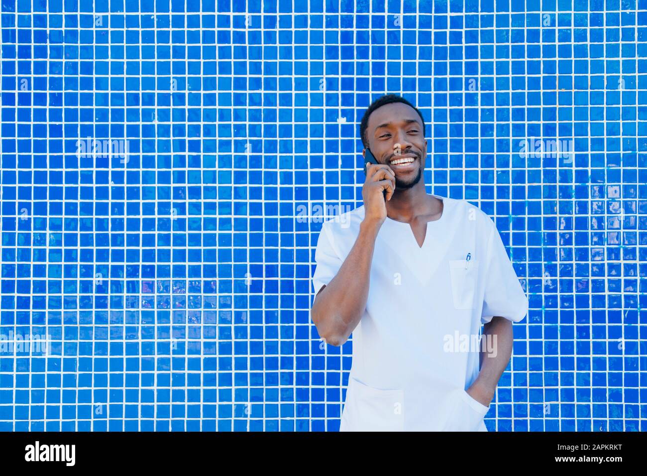 Portrait of laughing doctor on the phone standing against blue tiled ...