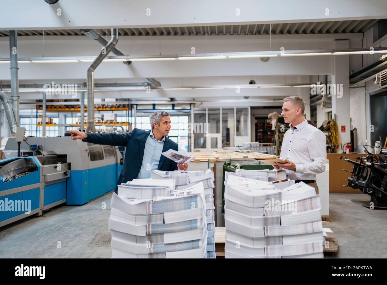 Two businessmen at stack of papers in a factory Stock Photo - Alamy