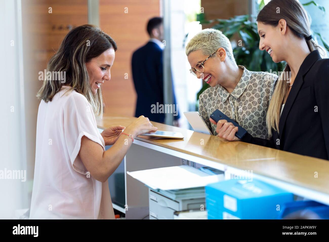 Two smiling businesswomen talking to woman at reception desk Stock ...
