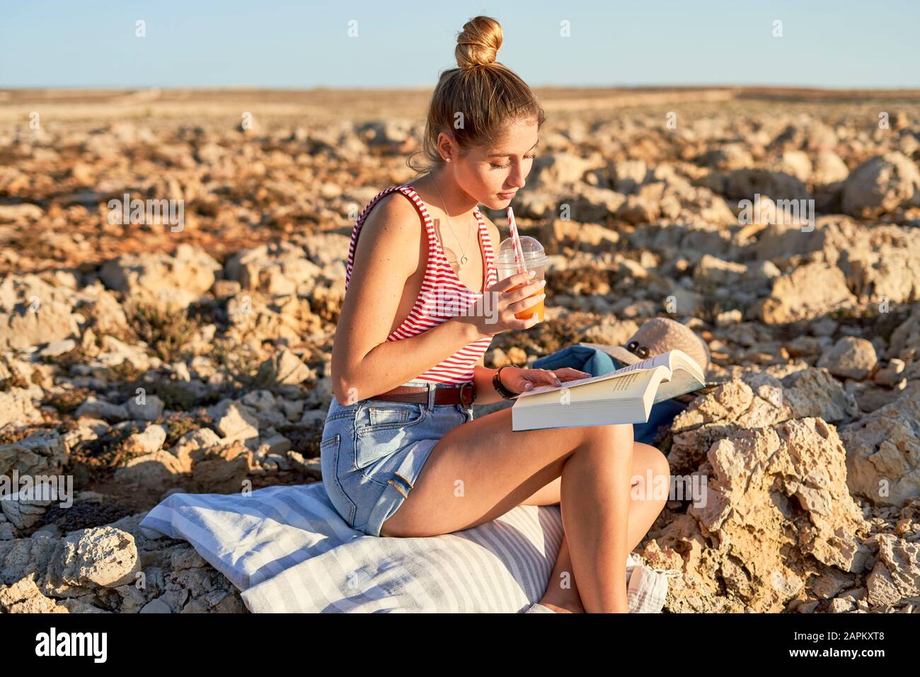 Young woman sitting on rocky beach, reading book Stock Photo - Alamy