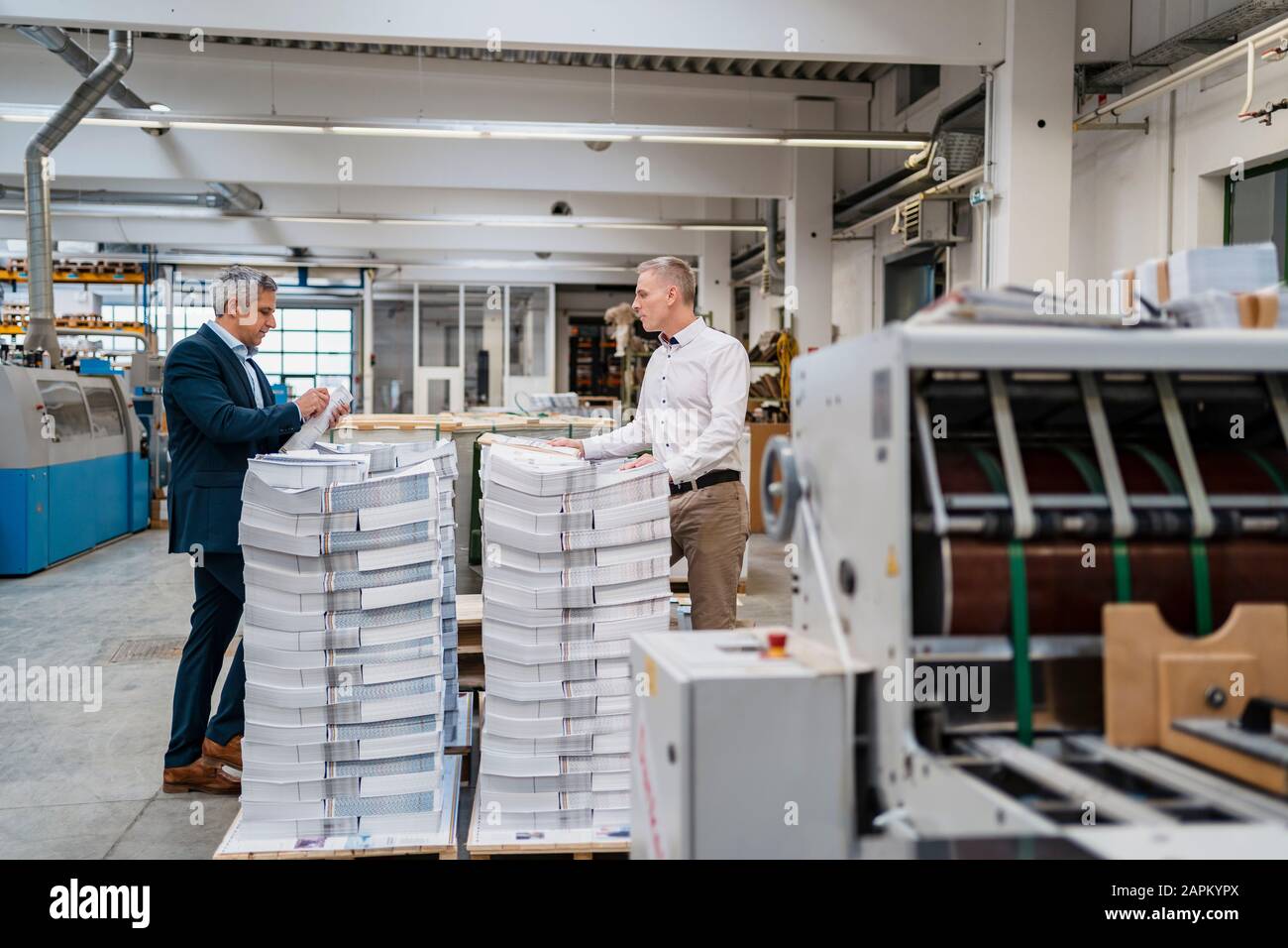 Two businessmen at stack of papers in a factory Stock Photo - Alamy