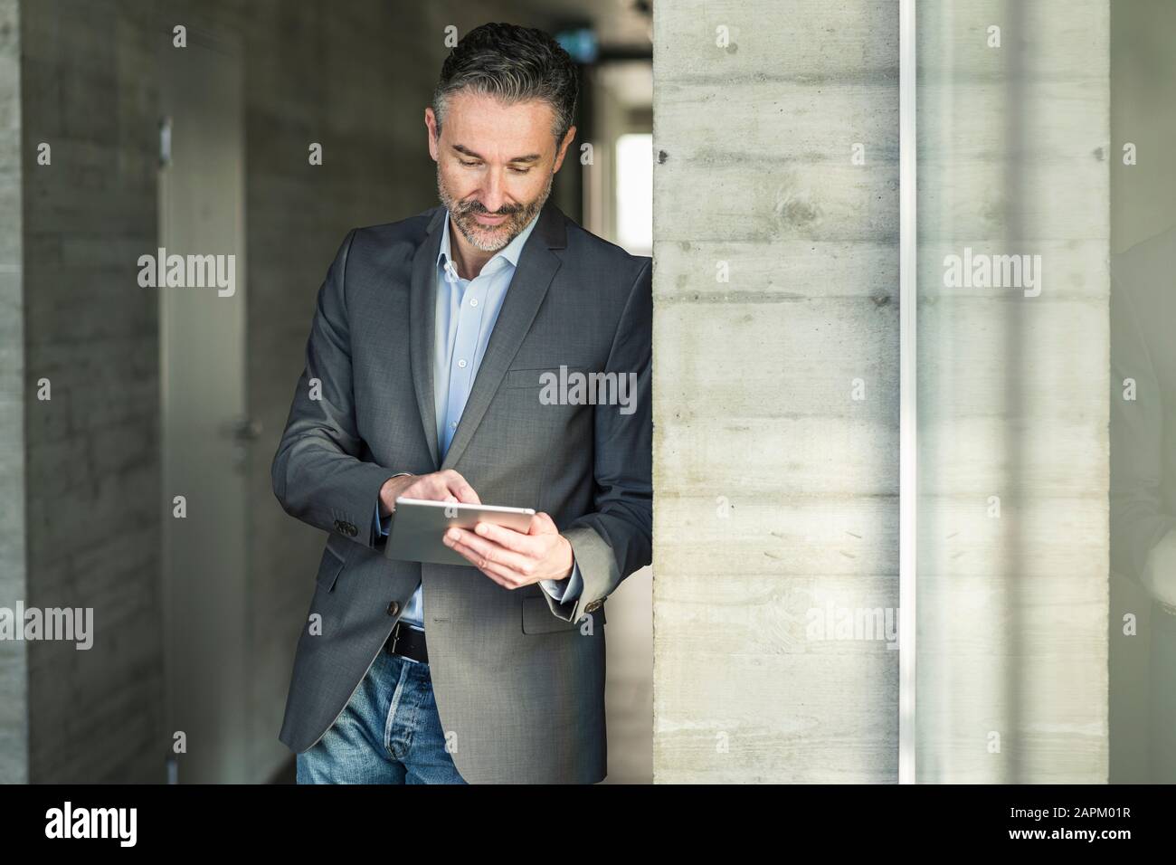 Mature businessman leaning against a wall in office using tablet Stock ...