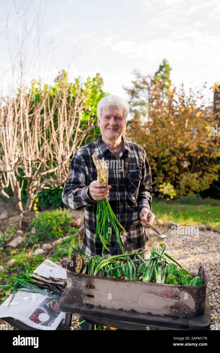 Portrait of proud senior man standing behind grill holding harvested ...
