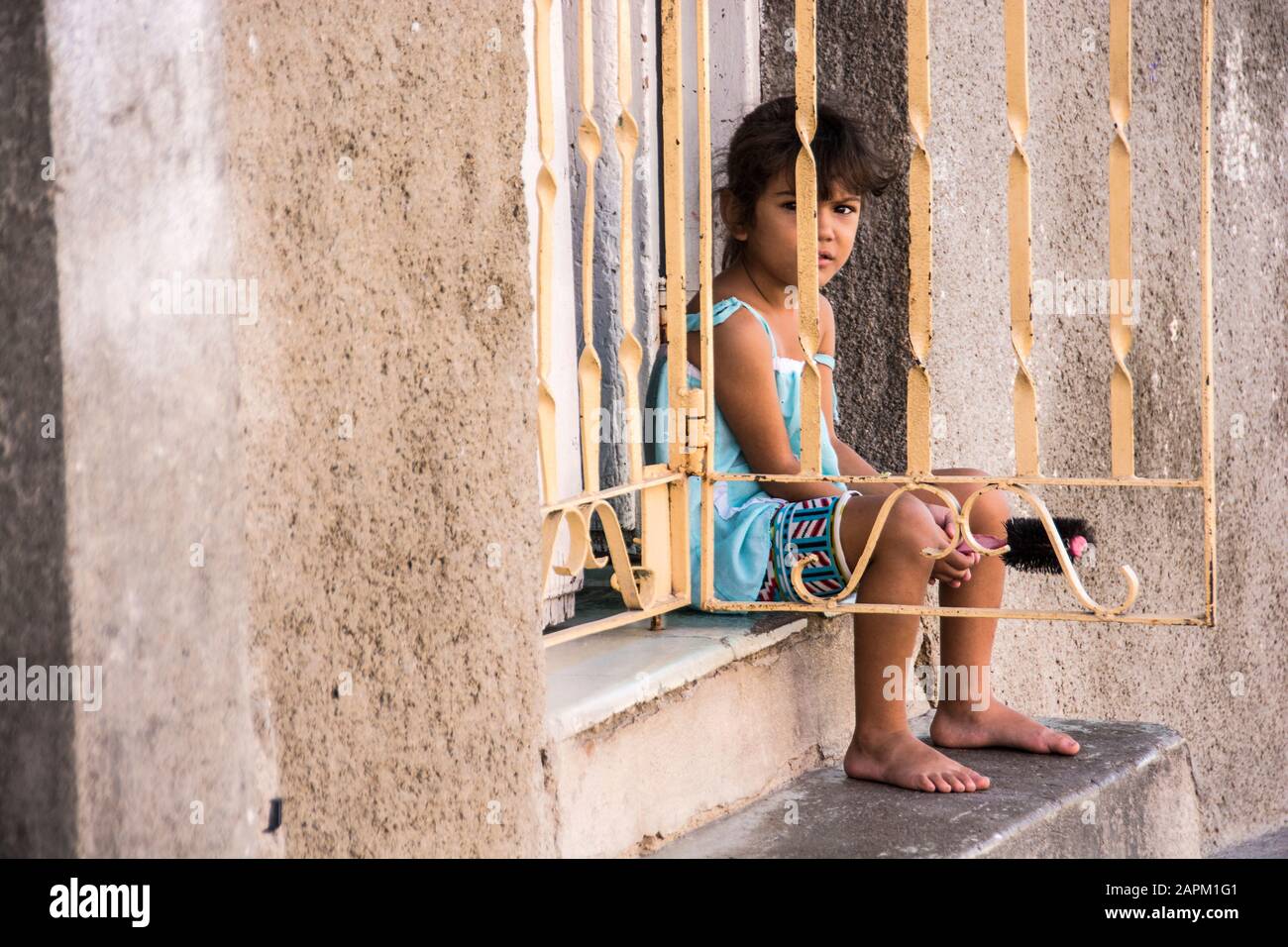 A cute, little, Cuban child sitting on the stoop of her home; Santiago ...