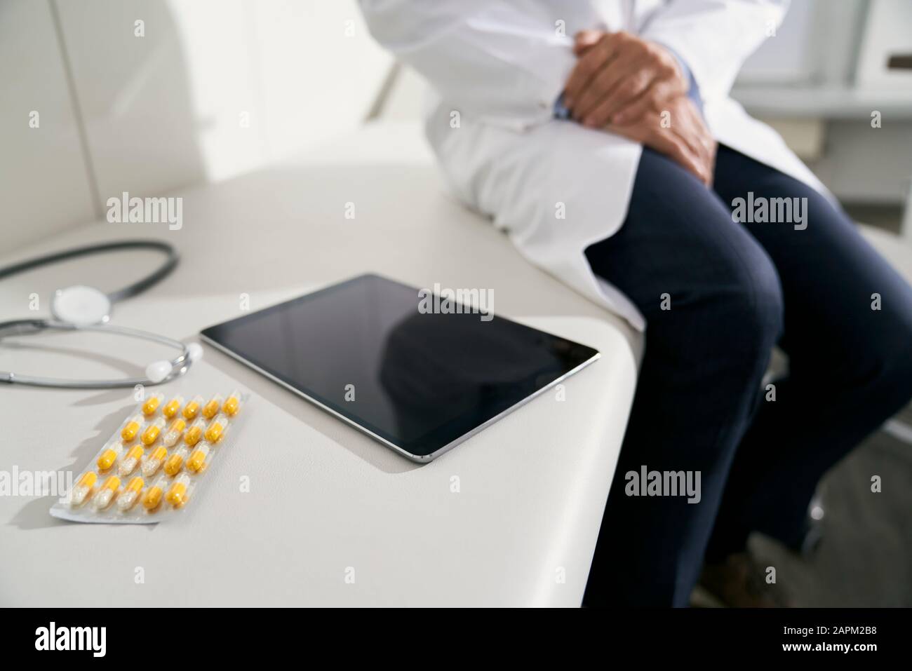 Doctor sitting on table in his medical practice with tablet ...