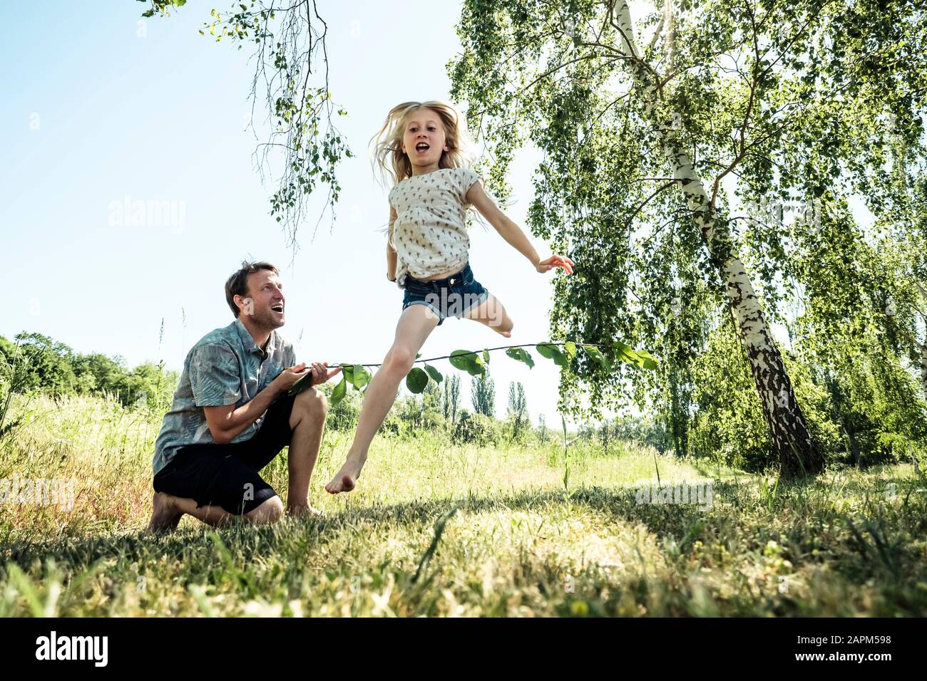 Father with daughter jumping over stick in poppy meadow Stock Photo - Alamy