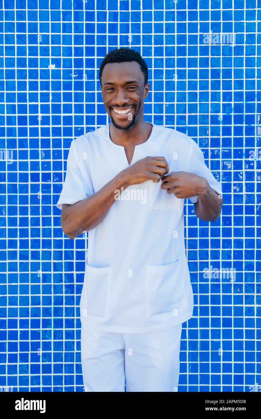 Portrait of laughing doctor standing against blue tiled wall Stock ...